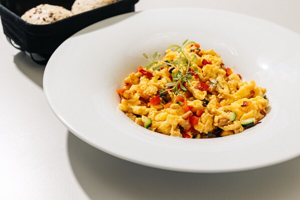 Um prato branco com ovos mexidos e legumes.