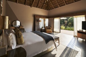 Quarto com uma cama grande, escrivaninha, cadeira, televisão e vista para o verde lá fora.