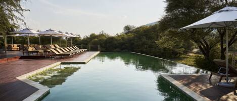 Uma piscina com espreguiçadeiras e guarda-sóis, cercada por árvores.