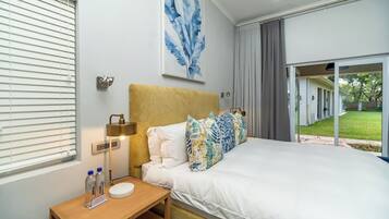 Quarto com cama, mesa de cabeceira, abajur e uma janela grande com persianas.