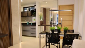 Uma cozinha moderna com área de refeições, apresentando uma mesa de vidro, cadeiras pretas e plantas em vasos.