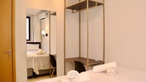 Quarto de hotel com uma cama, escrivaninha, cadeira e guarda-roupa.