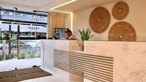 Uma área de recepção de hotel com design moderno, destacando um balcão de recepção em mármore, uma tela grande e arte de parede trançada decorativa.