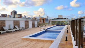 Uma área de piscina no terraço com espreguiçadeiras e vista para a cidade.