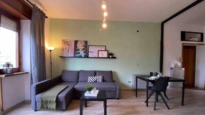 Uma sala de estar com sofá seccional, mesa de centro, mesa de jantar com cadeiras e um radiador.