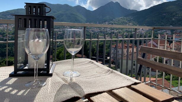 Duas taças de vinho vazias sobre uma mesa, com vista para uma montanha e uma cidade ao fundo.
