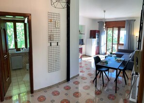 Uma sala de jantar com mesa e cadeiras, uma cozinha com geladeira e fogão, e uma sala de estar com sofá.