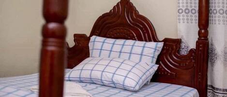 Uma cama de madeira com dossel, com colcha xadrez e almofadas a combinar.