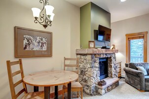 Uma sala de estar aconchegante com lareira de pedra, uma mesa redonda de madeira e um sofá confortável.