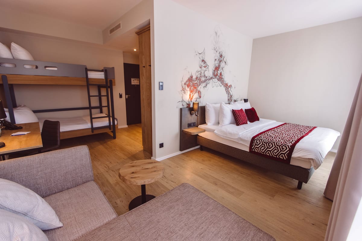 Quarto de hotel moderno com beliche, sofá, mesa pequena e um objeto decorativo na parede.