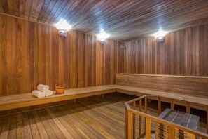 Uma sauna com paredes e bancos de madeira, chão de madeira e duas luzes fixadas na parede.