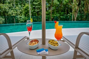 Uma mesa com duas bebidas, uma tigela de nozes e uma tigela de azeitonas, com vista para a piscina.