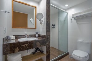 Um banheiro moderno com pia de mármore, um espelho grande, box de vidro e vaso sanitário branco.