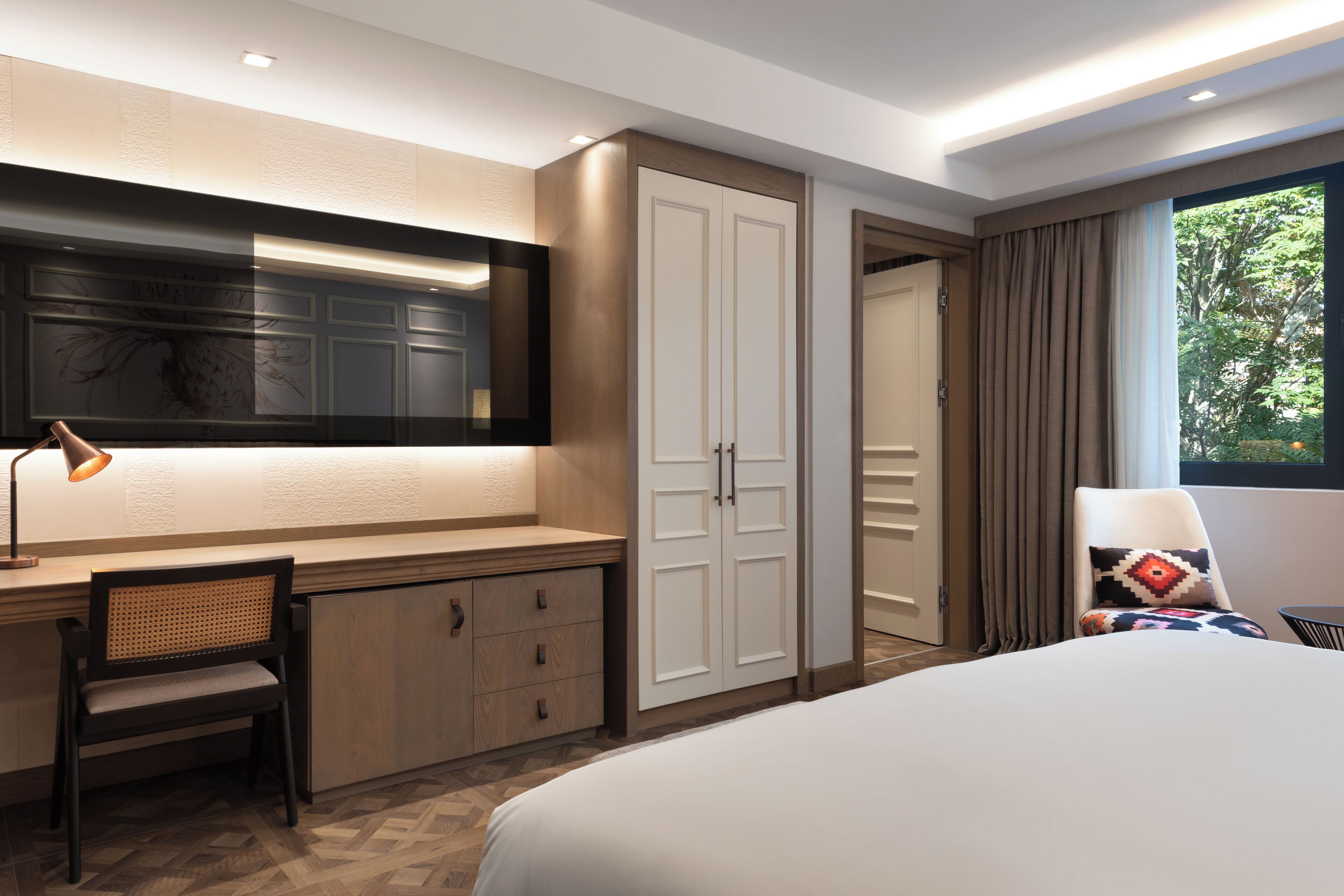 Quarto de hotel com cama, escrivaninha com cadeira, guarda-roupa e um espelho grande.
