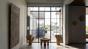 Um interior moderno com uma grande porta de vidro que dá para uma área externa, mobiliário de vime e um objeto decorativo na parede.