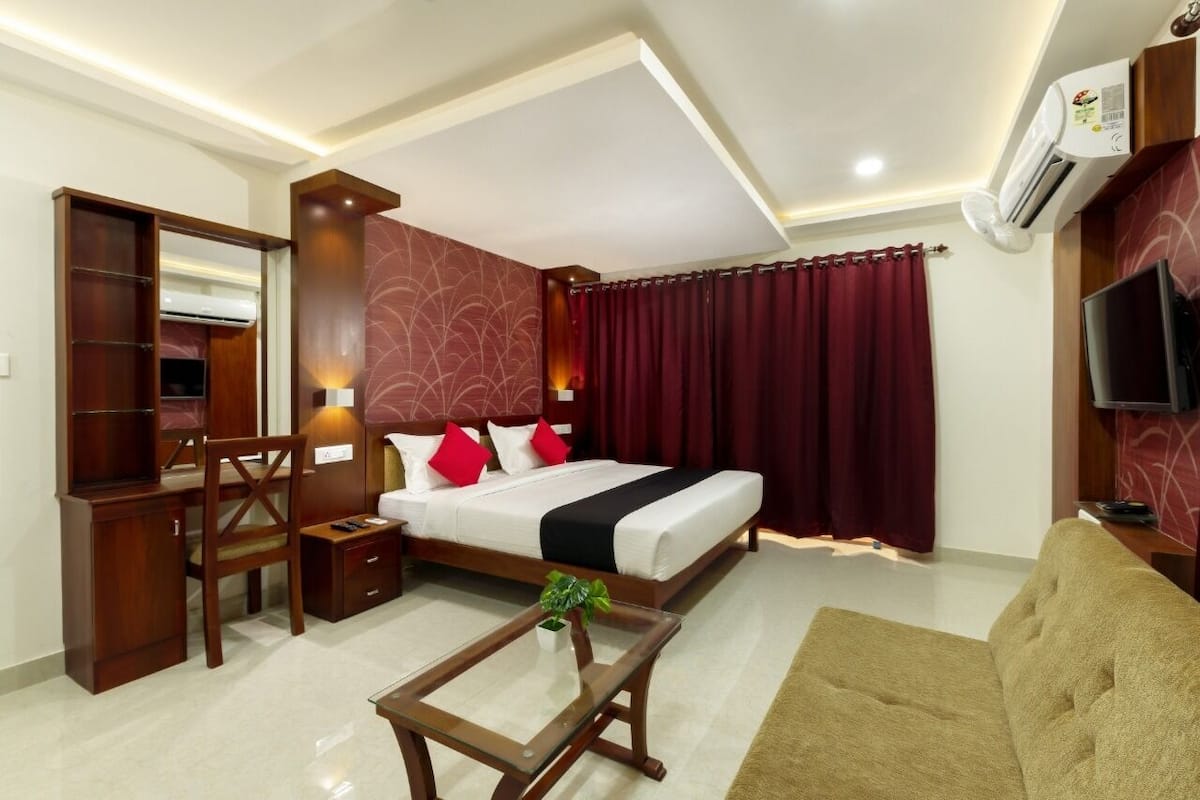 Quarto de hotel com cama, escrivaninha, cadeira, televisão e sofá.