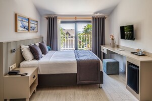 Quarto de hotel moderno com cama, mesa de cabeceira, escrivaninha e televisão.