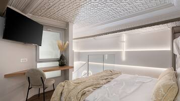 Quarto moderno com cama grande, televisão na parede, escrivaninha com cadeira e teto decorativo.