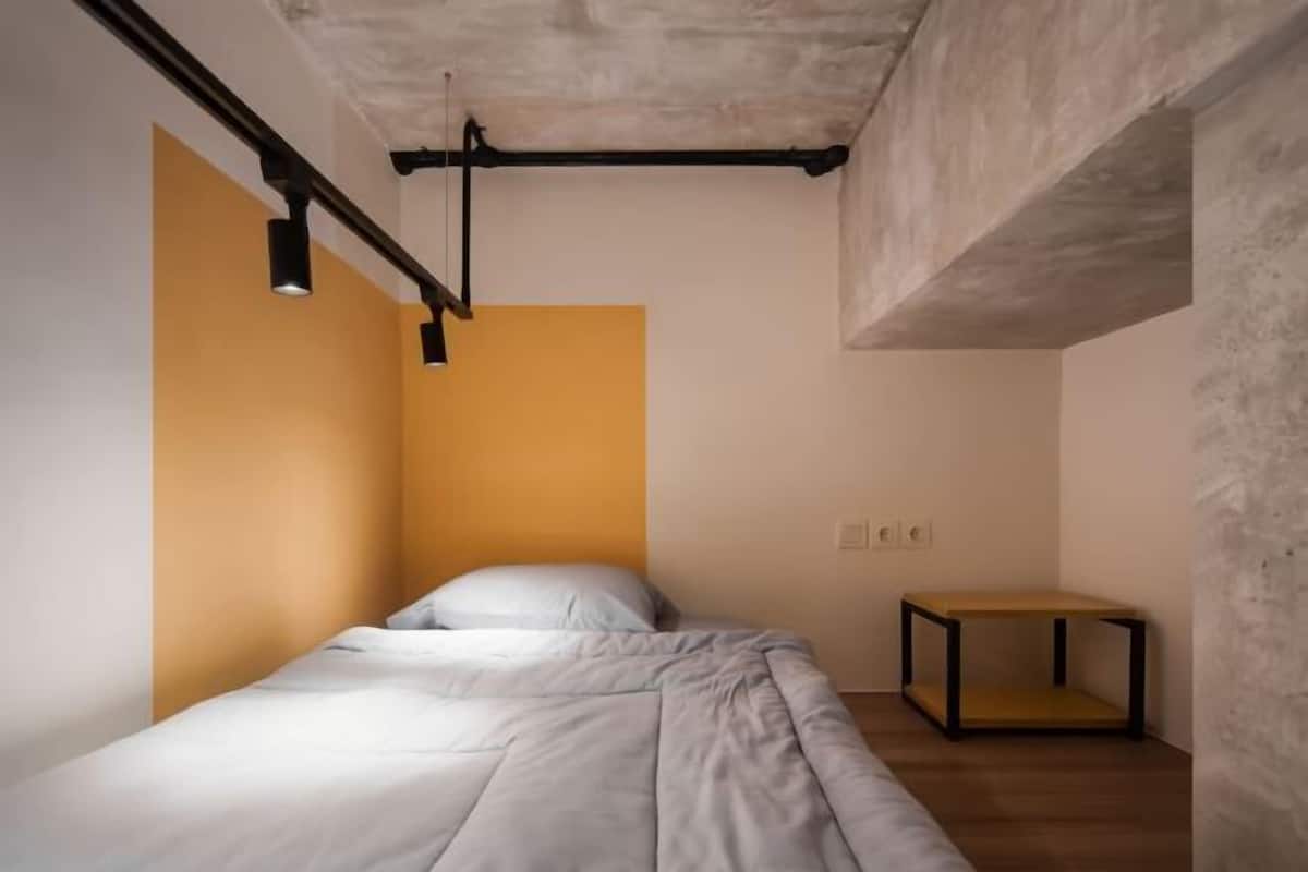Quarto com uma cama, uma mesa pequena e um lustre.