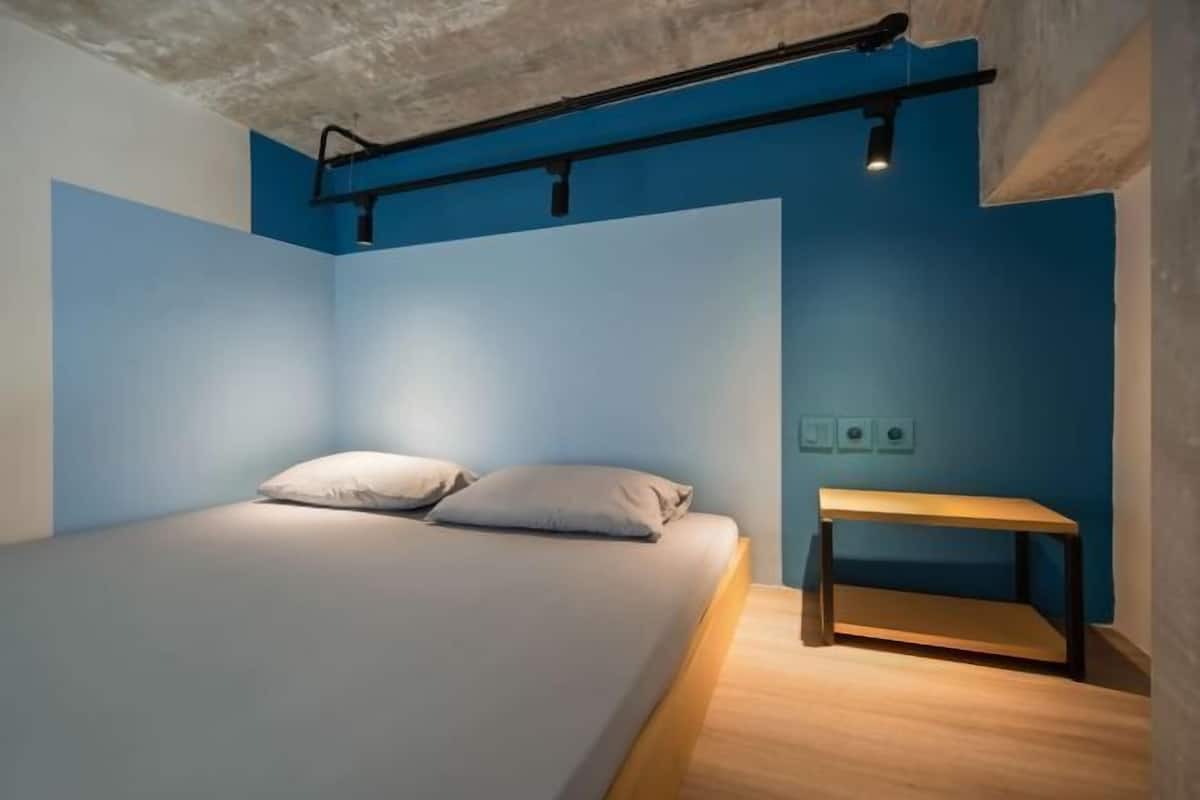 Quarto com cama, um banquinho e parede azul.
