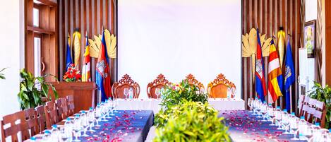 Uma longa mesa de banquete posta para um evento formal, com bandeiras e cadeiras de madeira de cada lado.