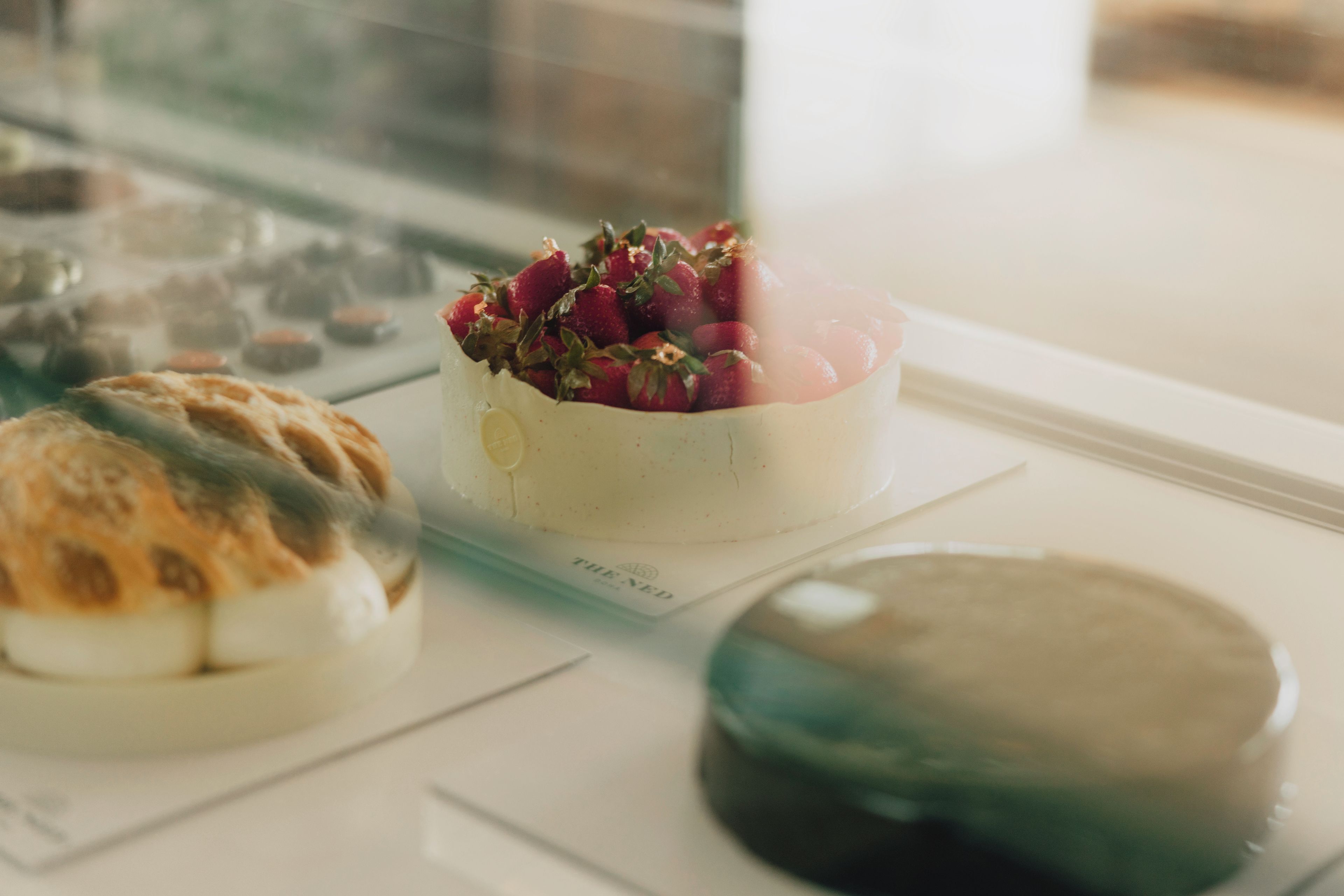 Exposição de sobremesas com diversos pastéis e uma taça de morangos.
