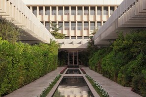 Um edifício moderno com um pátio central, rodeado por vegetação exuberante e um espelho d'água.