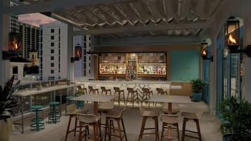 Um bar no terraço com um balcão comprido, vários bancos e vista para a paisagem urbana.