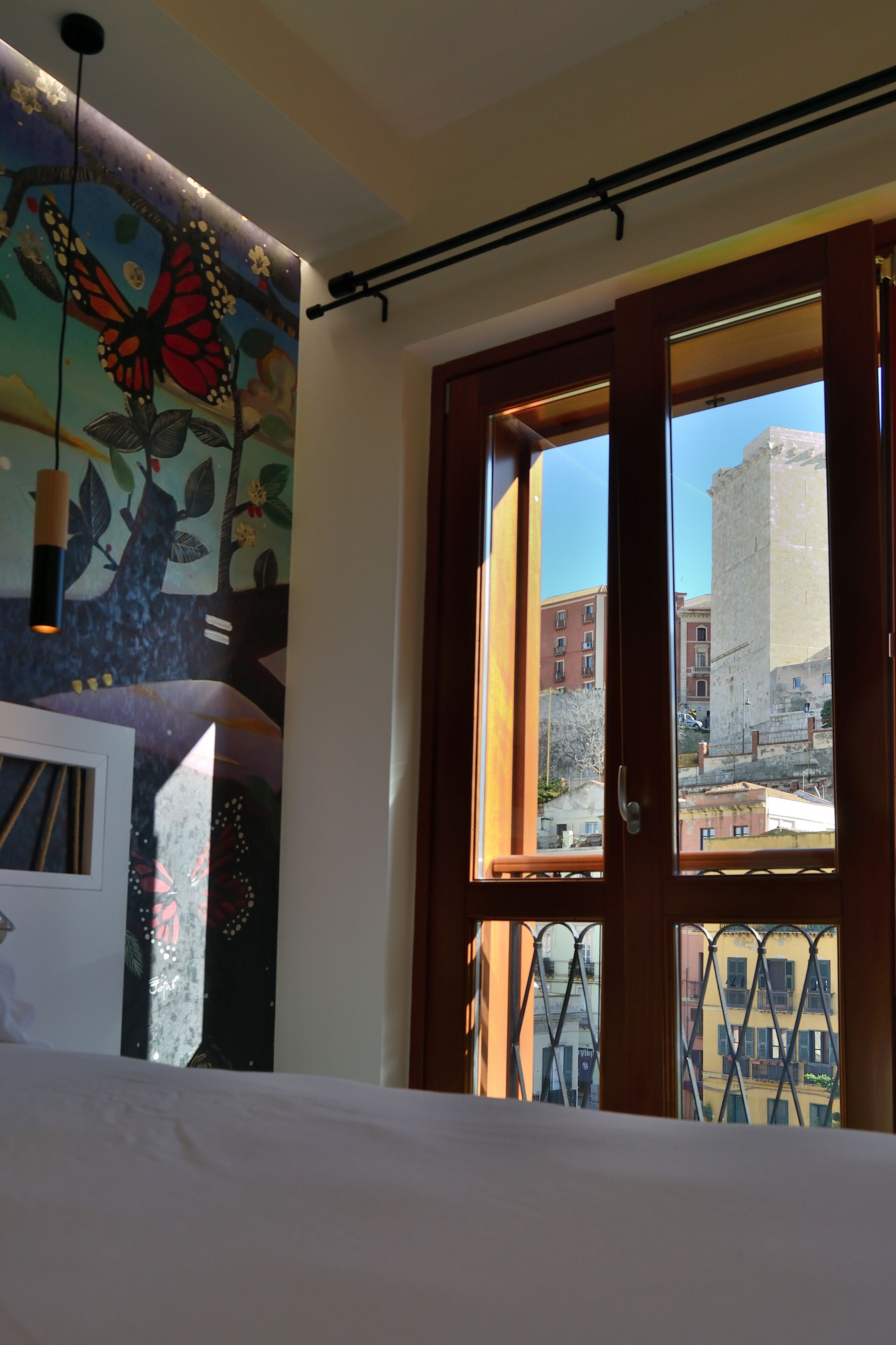 Quarto com uma grande janela, um mural com uma borboleta e vista para edifícios.