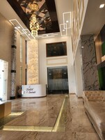 Um hall de hotel com balcão de recepção, um candelabro, piso de mármore e um sofá.