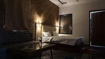 Quarto de hotel moderno com sofá, cama, mesa de centro de vidro e televisão na parede.