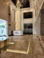 Um hall de hotel com balcão de recepção, piso de mármore, lustre e divisória de vidro.