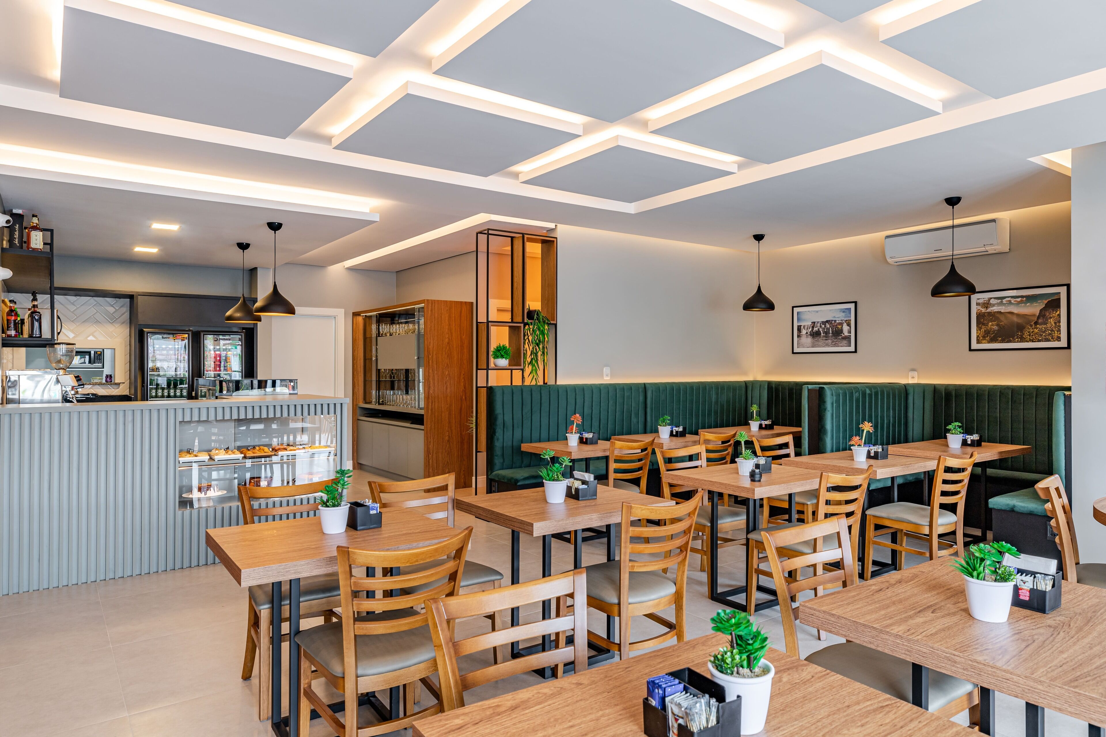 Um restaurante moderno com mesas e cadeiras de madeira, área de bar e um espaço com assentos em um estante verde.