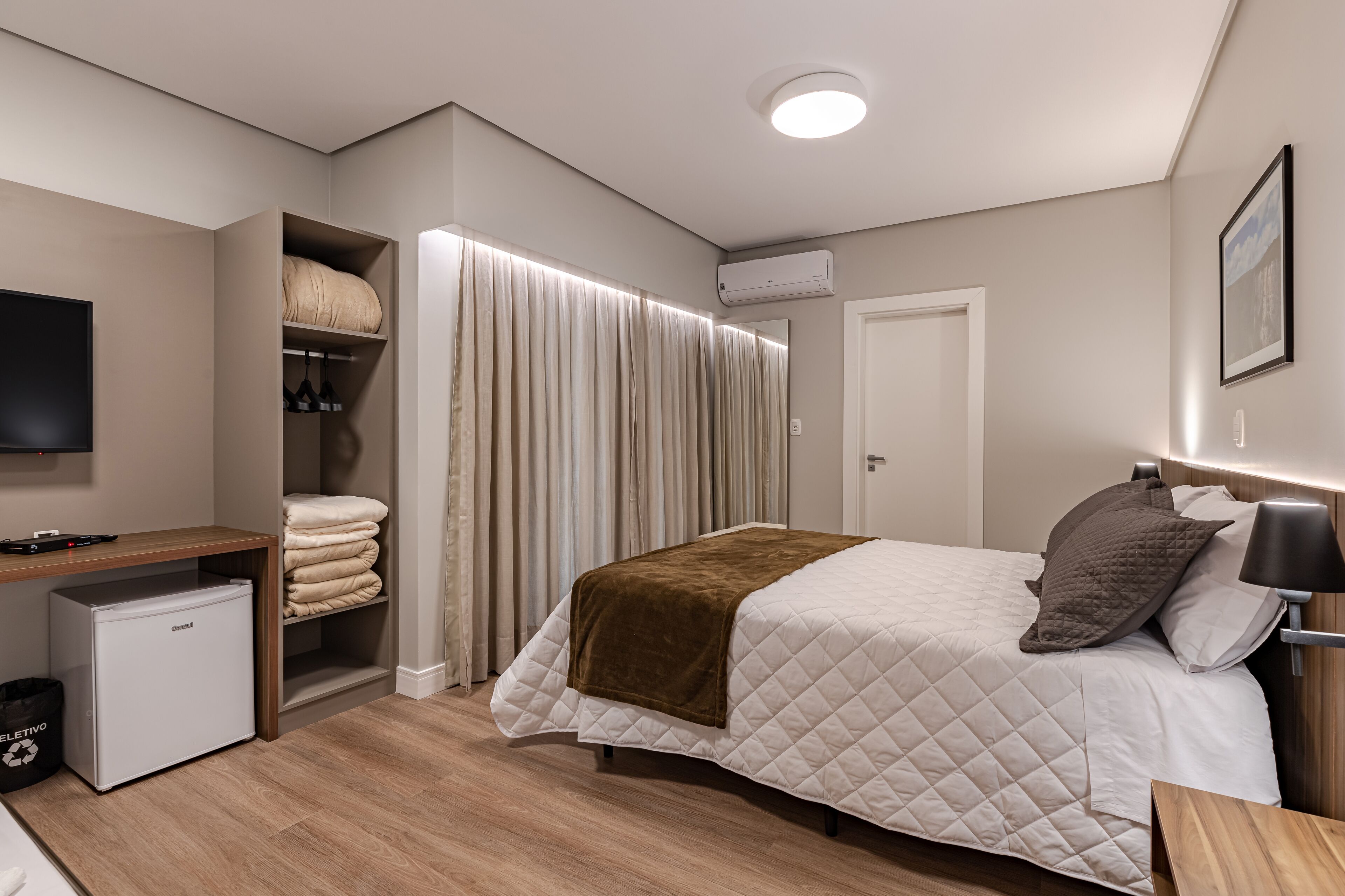 Quarto moderno com cama, mesa de cabeceira e um pequeno frigorífico.