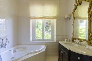 Casa de banho com banheira, toucador com espelho e janela com cortinas.