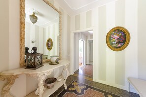 Um corredor com um espelho grande e um console ornamental branco e dourado, e um quadro floral na parede.
