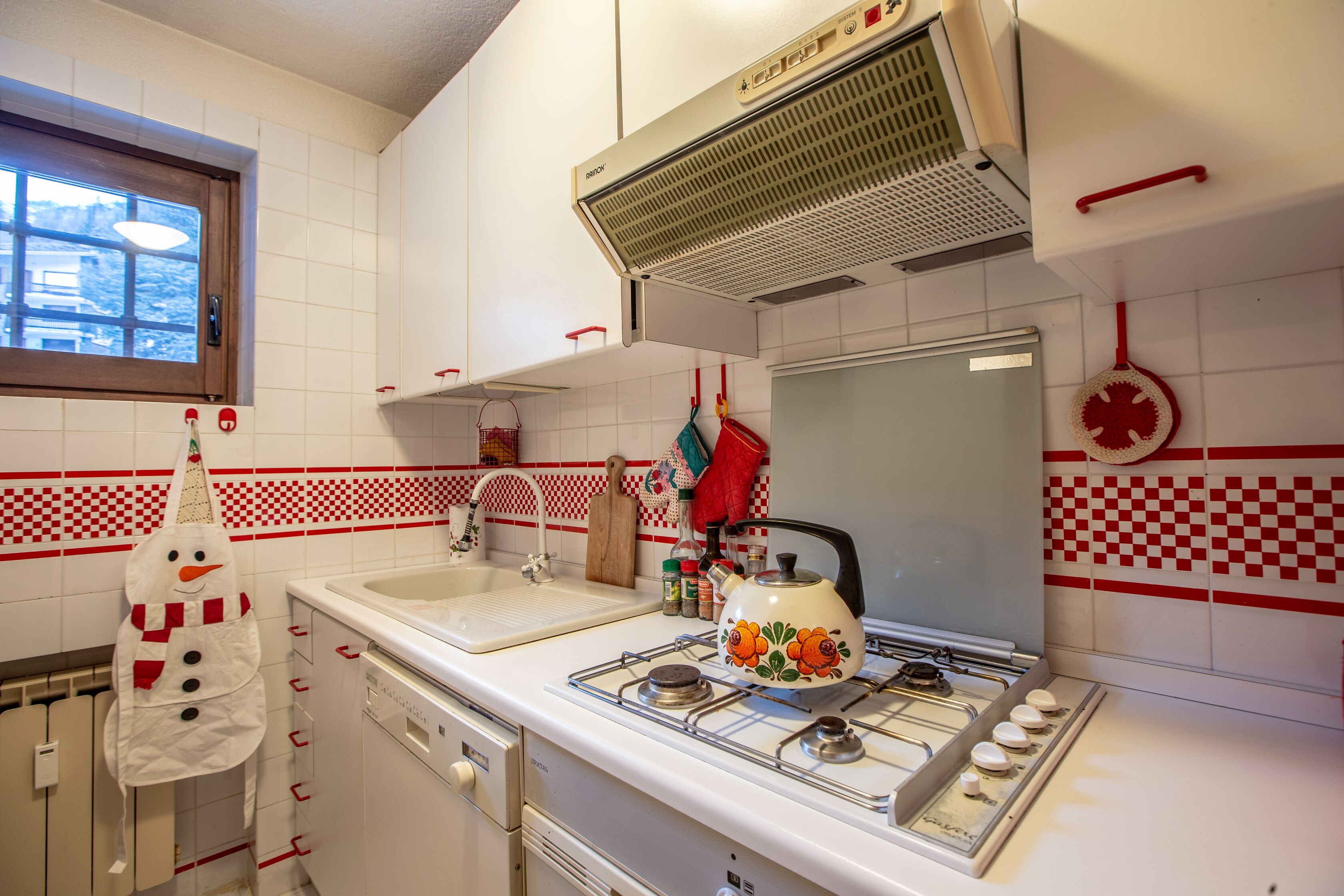 Cozinha com armários brancos, fogão e janela com vista para árvores.