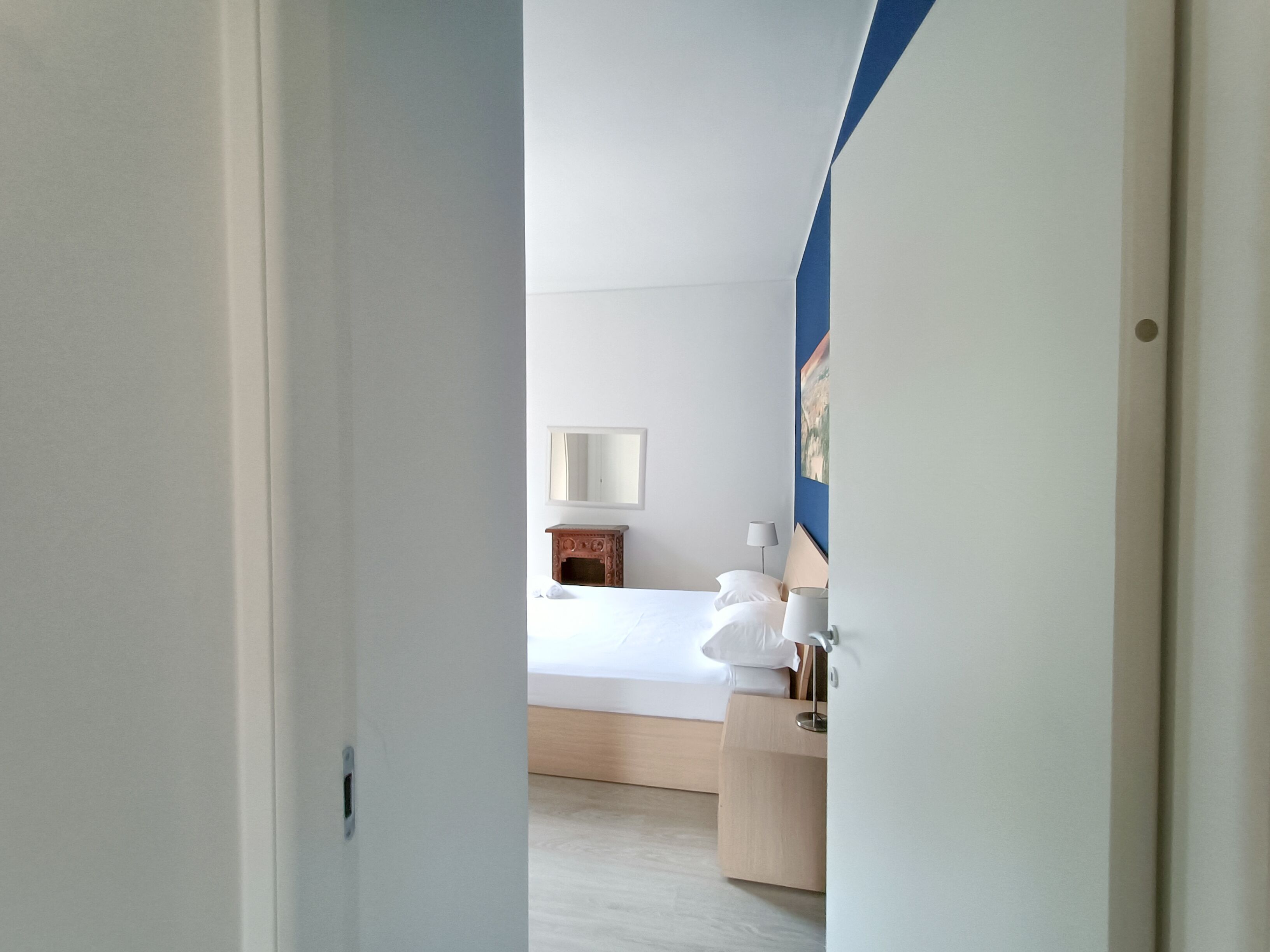 Quarto de hotel com uma cama, mesa de cabeceira, abajur e um quadro na parede.