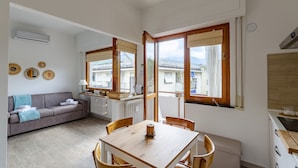Sala de estar moderna com sofá, mesa de jantar e cadeiras. Há uma cozinha com fogão e uma janela com vista para o exterior.