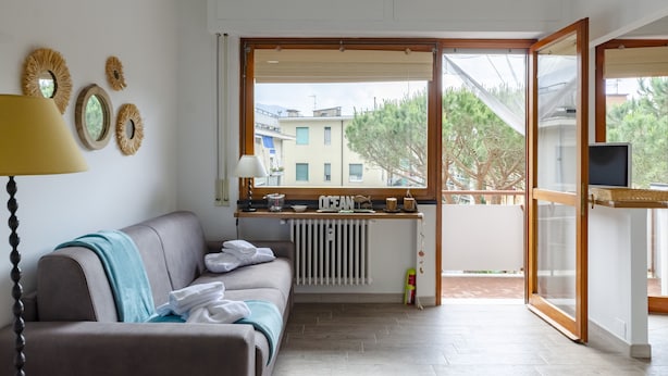 Uma sala de estar moderna com sofá, luminária, radiador e janela com vista para edifícios e árvores.