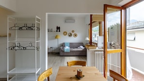 Um quarto com uma mesa de jantar, cadeiras, um sofá, um cabideiro e uma janela com vista para edifícios.