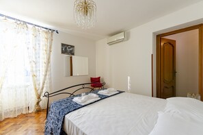 Quarto de hotel com cama, uma cadeira vermelha, um candelabro e um aparelho de ar condicionado.