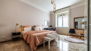 Quarto com cama, mesas de cabeceira, escrivaninha, cadeira, janela e espelho.