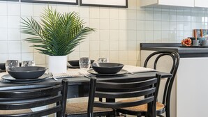 Uma área de refeições com uma mesa posta para dois, com cadeiras pretas e um vaso de planta.