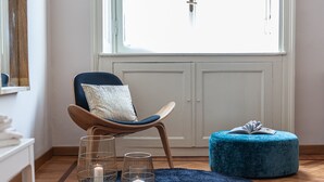 Um quarto com uma cadeira de madeira, um banquinho redondo e um tapete azul escuro.