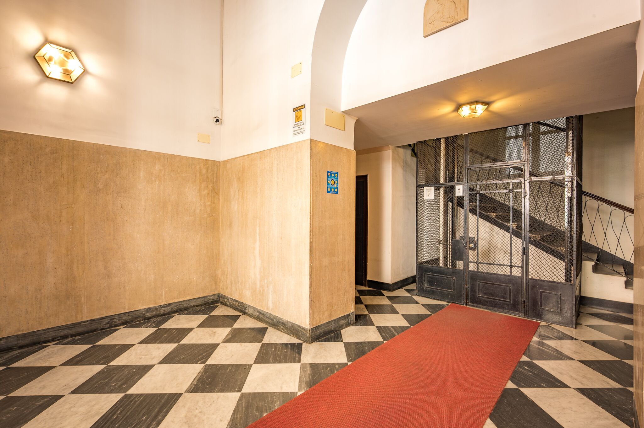 Um corredor com piso xadrez, tapete vermelho e escada com corrimão de metal.