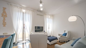 Uma sala de estar moderna com televisão, sofá, poltrona e mesa de jantar.