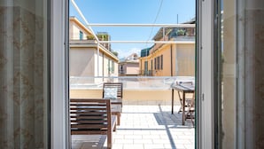 Vista de varanda com mesa e cadeiras, piso de azulejos e edifícios ao fundo.