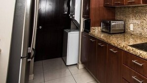 Uma cozinha compacta com armários de madeira, geladeira de aço inoxidável, micro-ondas e torradeira.