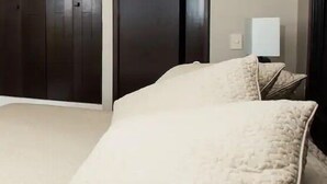 Quarto de hotel com cama, mesa de cabeceira, luminária, ventoinha no teto e armários de madeira escura.